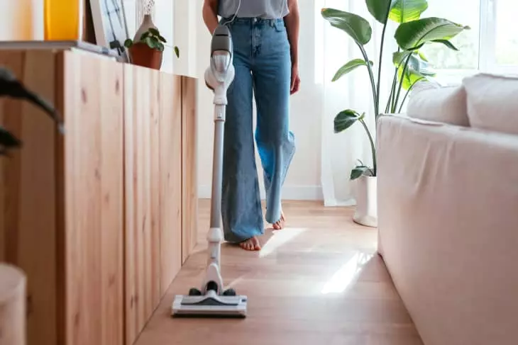 umuntu muri jeans vacuuming laminate hasi, idirishya nigiti kirekire inyuma ye