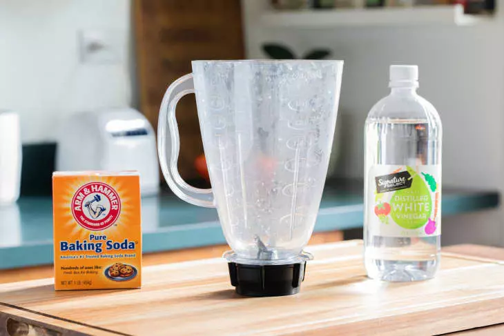 Blender dengan bekas plastik keruh, dengan kotak baking soda dan botol cuka putih, di atas kaunter dapur