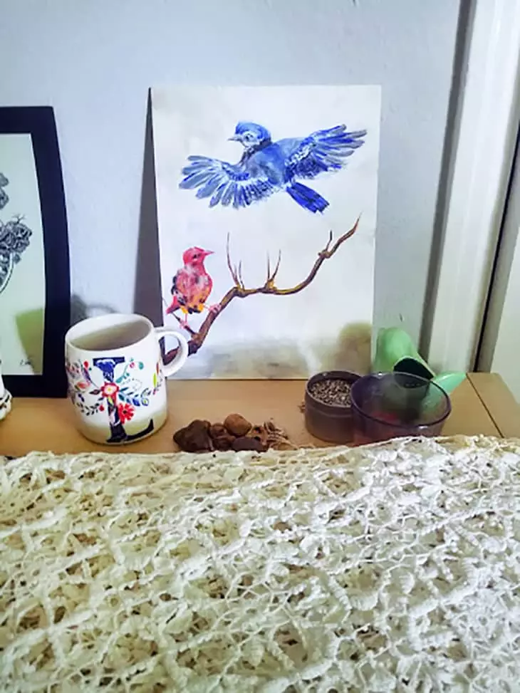 Nakatupi ang isang tablecloth sa isang kahoy na istante, na napapalibutan ng mug, isang painting, at ilang iba pang mga trinket.