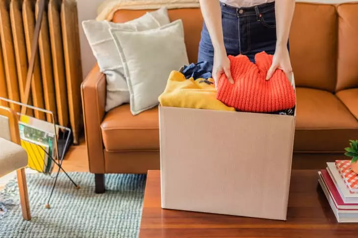 kartonnen doos met iemand die kleren op de salontafel legt