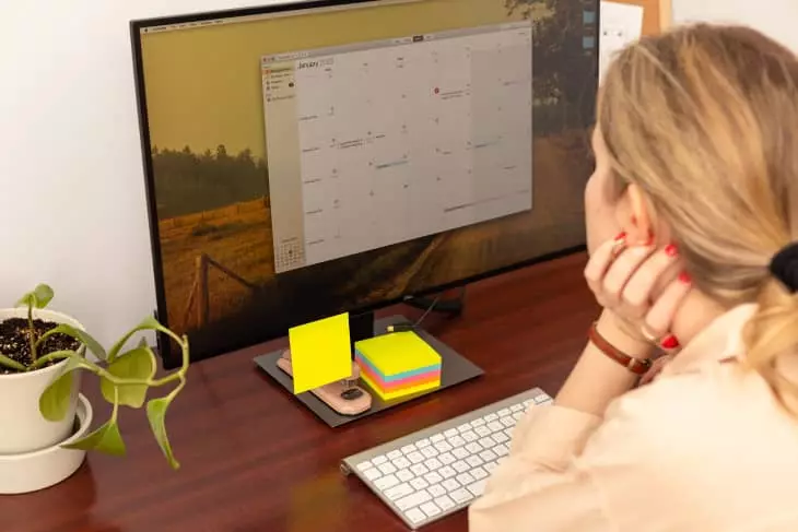 En kvinna som sitter vid ett datorbord och granskar en digital kalenderapp