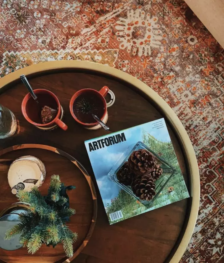 Close-up sa coffee table nga adunay mga mug, pinecone, greenery, ug libro