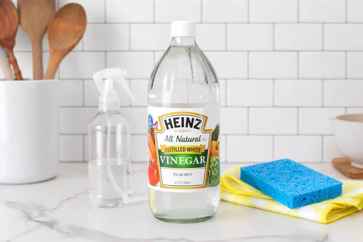 En flaska Heinz destillerad vit vinäger på en köksbänk bredvid svampar, en rengöringsduk och en sprayflaska