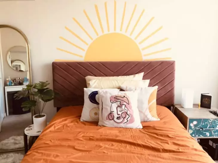 Oranssi sänky, jonka takana seinään maalattu aurinko