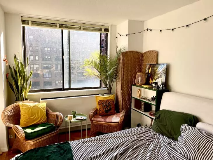 Makuuhuone raidallinen sänky, korituoli ja kasveja ikkunan vieressä