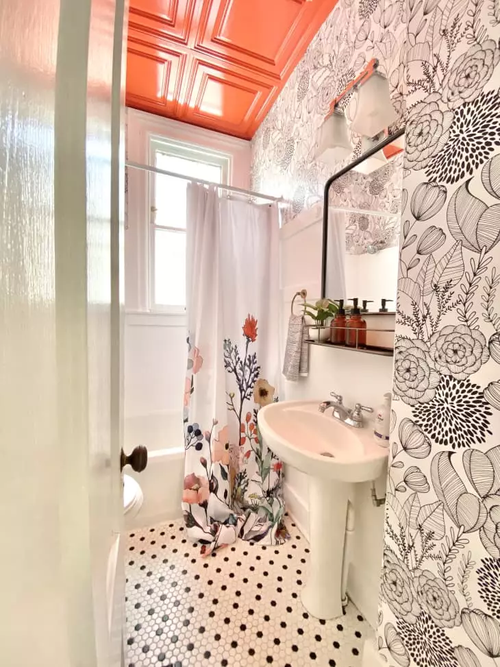 Baño con papel tapiz floral, cortina de ducha floral y techo naranja