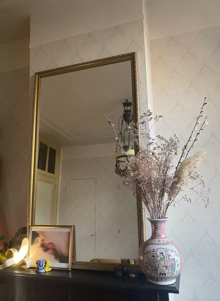 Stačiakampis veidrodis, vaza ir nedidelis įrėmintas meno kūrinys ant atbrailos