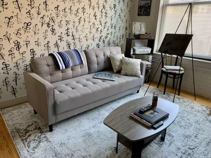 Stue med grå sofa, staffeli og svart og hvitt håndmalt veggmaleri bak sofaen