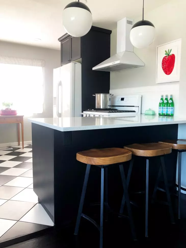 Virtuvė su juodai baltomis šachmatų lentomis ir dviem dideliais sferiniais pakabinamais šviestuvais