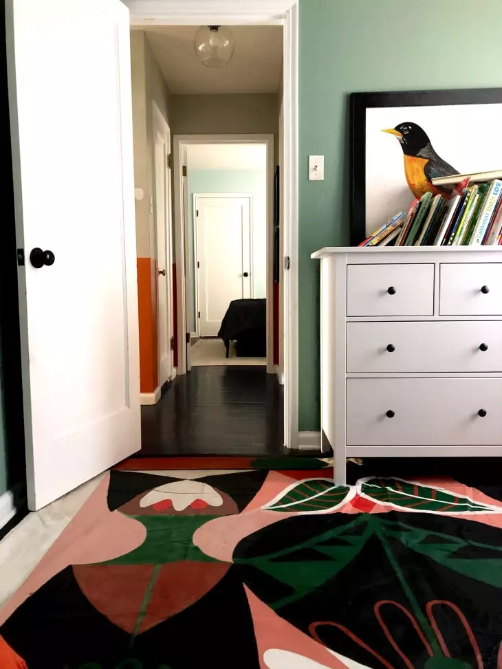 Izba so zelenými stenami, bielou komodou, umeleckými dielami vtákov a grafickým kobercom