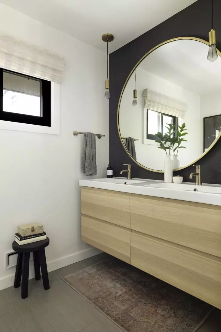 Juodas, baltas ir neutralus vonios kambarys su dideliu apvaliu veidrodžiu