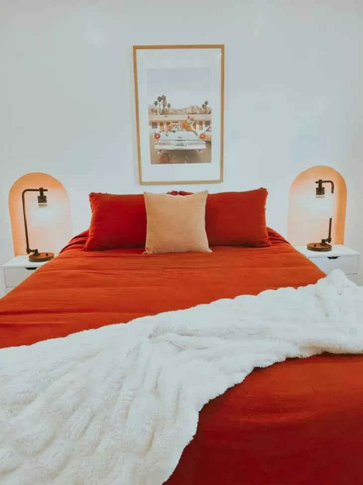 Dormitori amb roba de llit vermella i arcs pintats darrere taules auxiliars
