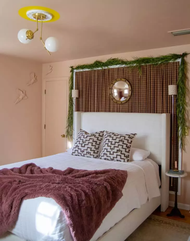 Kamar tidur dengan dinding merah muda muda dan karangan bunga hijau di sekitar kepala tempat tidur