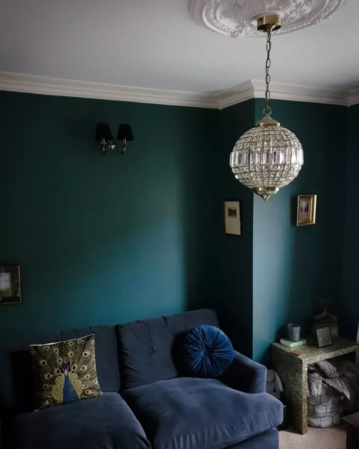 Stue med dypgrønne vegger, en marineblå sofa og en glamorøs pendel