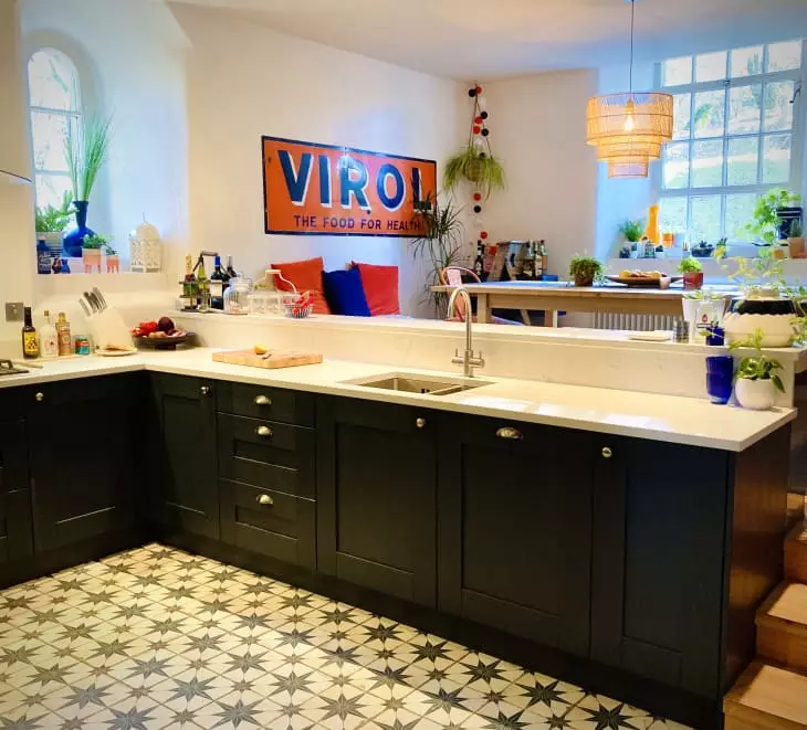 Dapur dengan jubin bercorak bintang, kabinet hitam dan pemandangan ke ruang makan dengan loket rotan dan papan tanda logam grafik