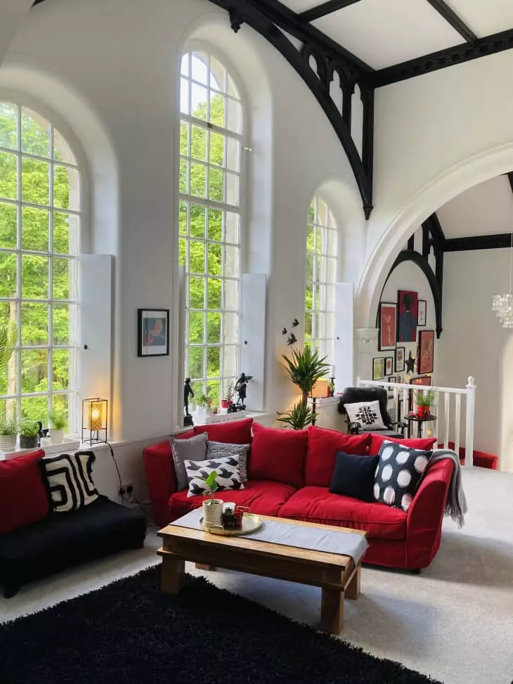 Dzīvojamā istaba ar sarkanu dīvānu, augstiem griestiem un arkveida logiem