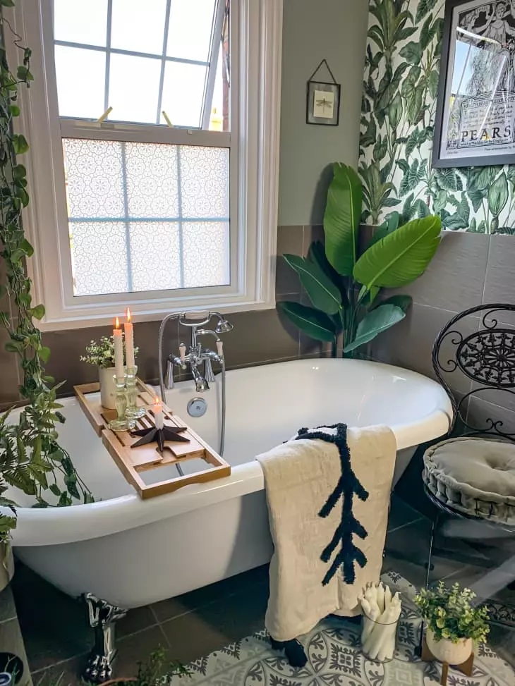 Wanna Clawfoot w łazience z dużą ilością roślin i zielono-białą tropikalną tapetą