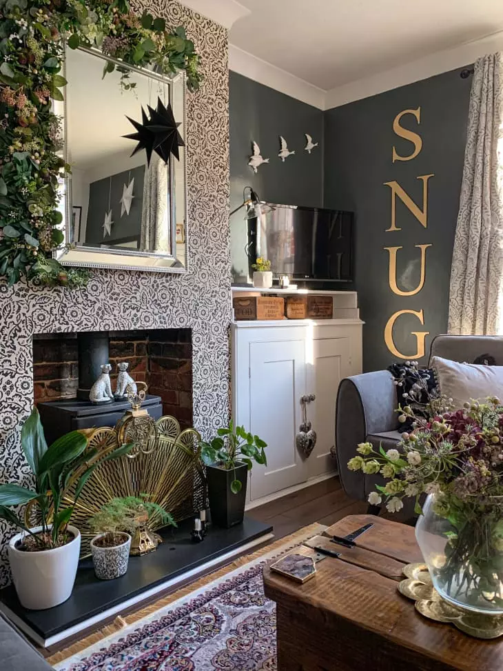 Vardagsrum med blommig detalj på öppen spis och bokstäver som stavar SNUG hängande på väggen