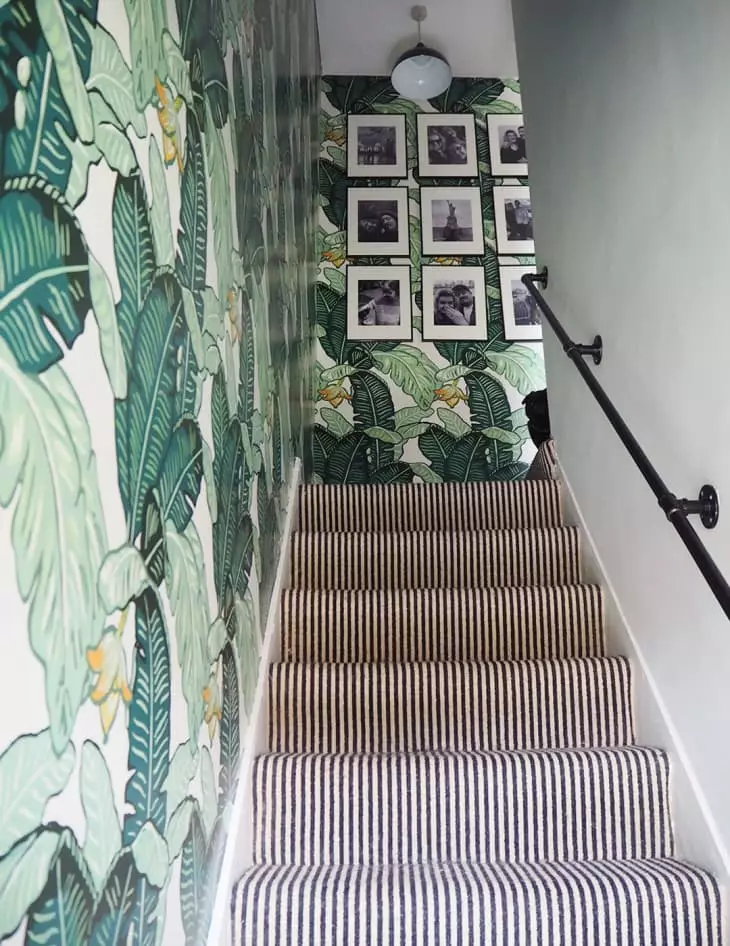 Escalera con moqueta a rayas en los escalones y papel tapiz de hojas de palma