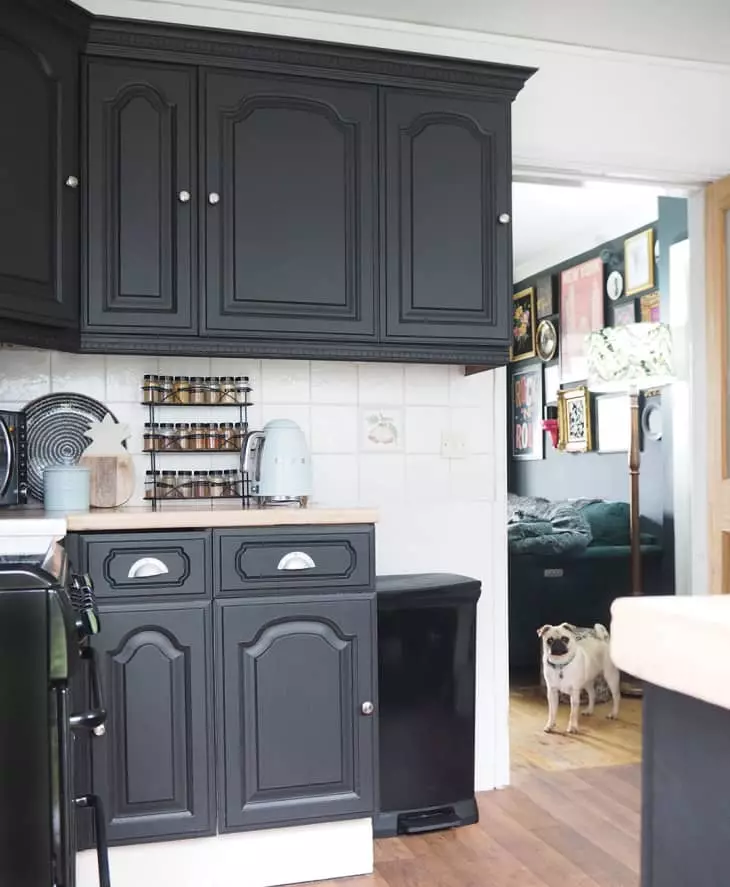 Kuhinja s ugljeno sivim ormarićima, bijelim kvadratnim pločicama i stalkom za začine na pultu