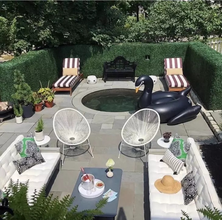 Espace patio orné de canapés et de chaises blancs, de chaises longues à rayures et d'un flotteur de piscine en forme de cygne noir