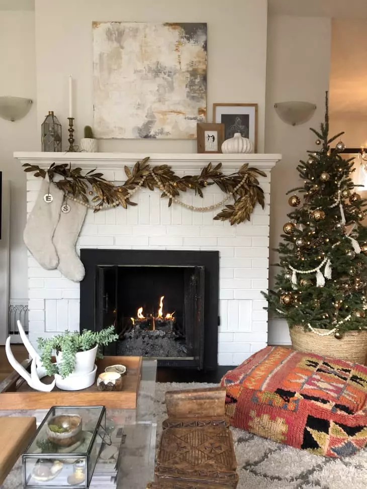 Salón bohemio con árbol de Navidad junto a una chimenea adornada con guirnaldas y medias