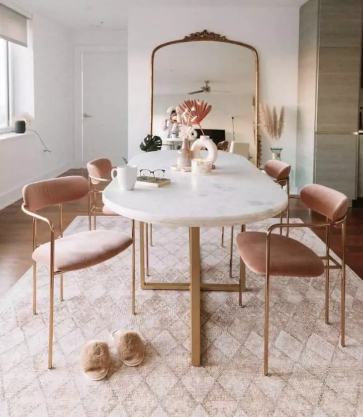 Sala de jantar com mesa de mármore e detalhes em dourado e blush