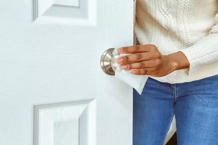 Жена почиства дръжката на вратата с дезинфекционна кърпа