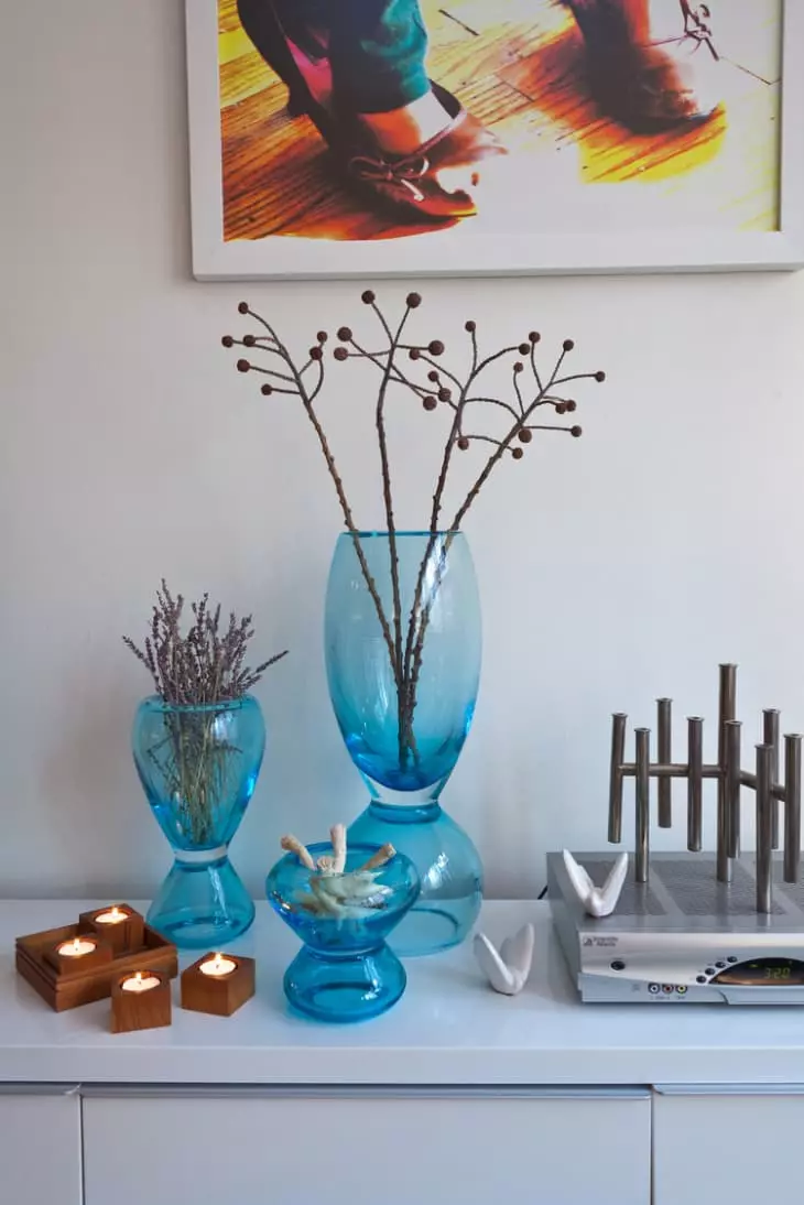 Três vasos de vidro azul cheios de flores secas em cima de um armário branco moderno